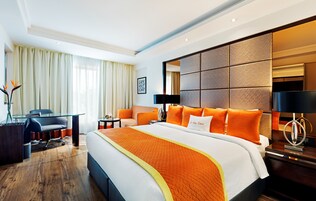 Quarto de hotel com cama grande, escrivaninha, cadeira e vista da cidade.