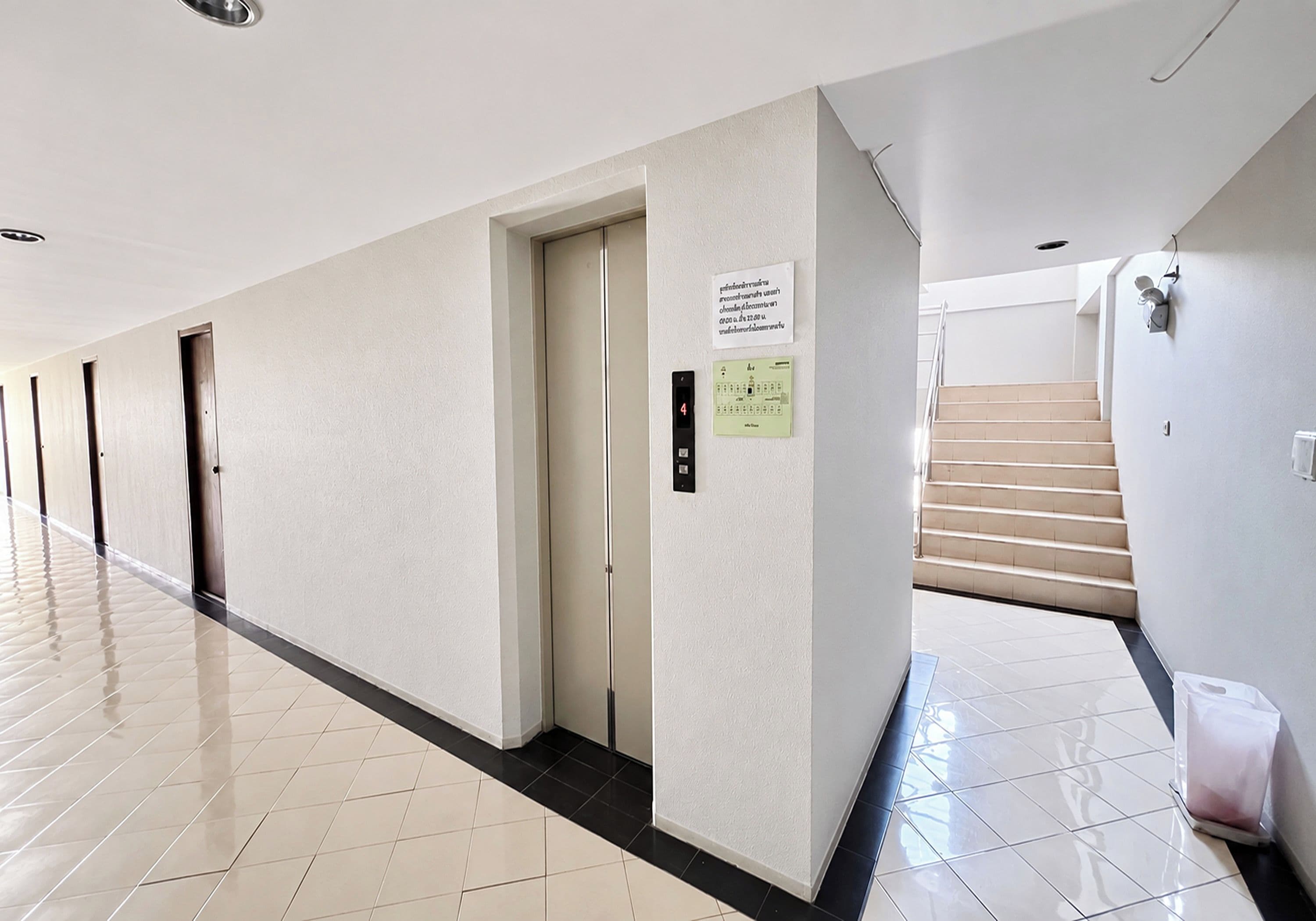 Corredor de hotel com piso de azulejos, um elevador fechado e escadas que levam a outro andar.