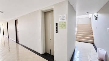 Corredor de hotel com piso de azulejos, um elevador fechado e escadas que levam a outro andar.