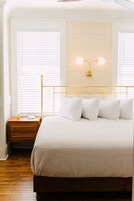 Quarto com cama, mesa de cabeceira e luminária na parede.