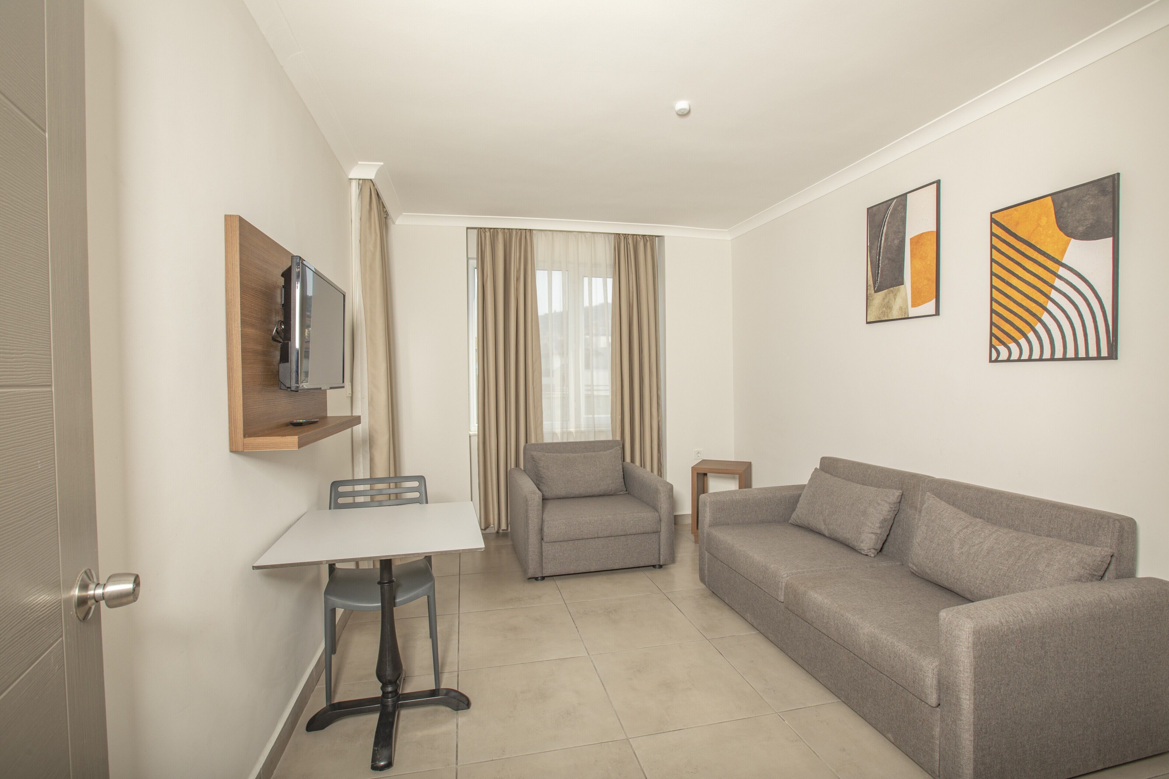 Uma sala de estar moderna com um sofá, poltrona e uma TV sobre uma estante de madeira.