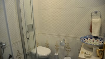 Casa de banho com cabine de duche em vidro, sanita, lavatório com bacia decorativa e um porta-toalhas.