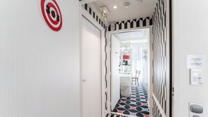 Um corredor com piso de padrão geométrico, um sinal de alvo na parede e uma porta que dá para um quarto com um cabideiro.