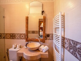 Um banheiro com parede revestida de azulejos bege, um espelho grande, uma pia com cuba, um porta-toalhas e um vaso sanitário.