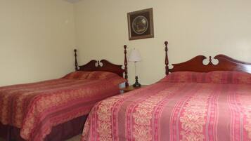 Duas camas de solteiro com cabeceiras de madeira e roupa de cama vermelha combinando em um quarto com paredes lisas e um quadro emoldurado sobre as camas.