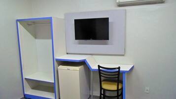 Quarto pequeno com escrivaninha, cadeira e televisão fixada na parede.
