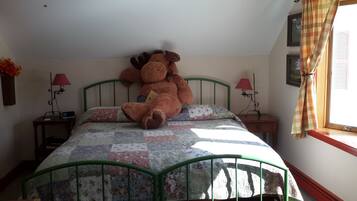 Uma cama com um edredom estampado com flores, duas luminárias de cabeceira e um urso de pelúcia grande.