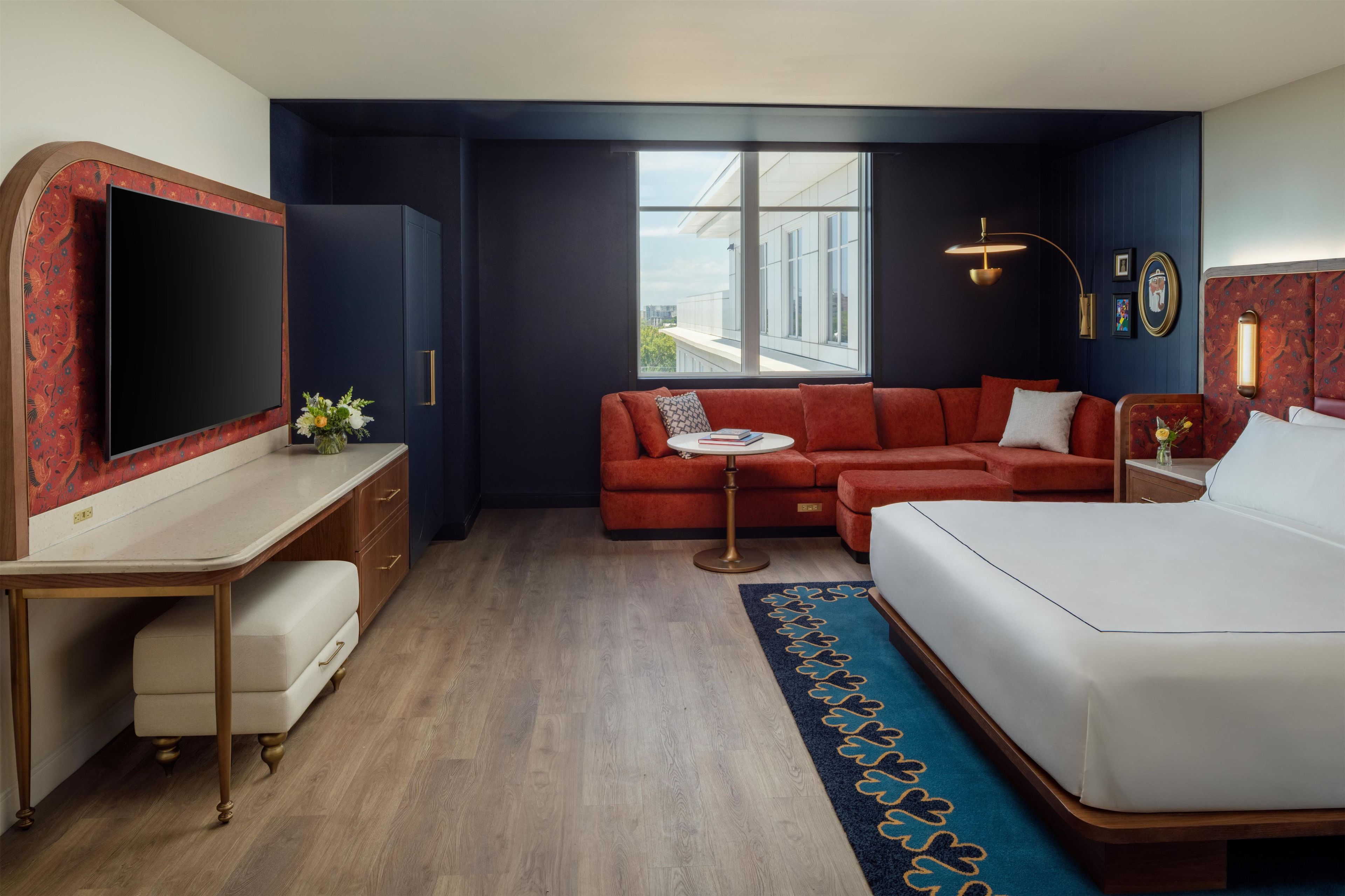 Quarto de hotel moderno com uma cama grande, um sofá, uma escrivaninha e uma televisão.