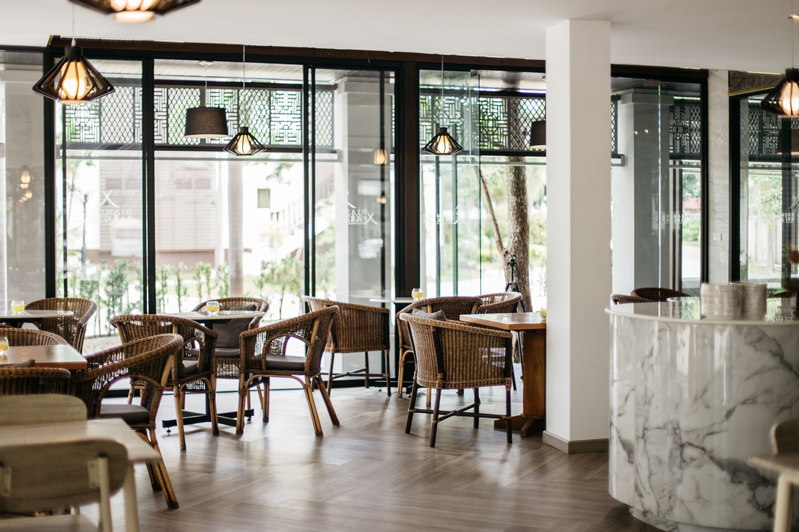 Interior de restaurante com móveis de vime, janelas amplas e luminárias pendentes.
