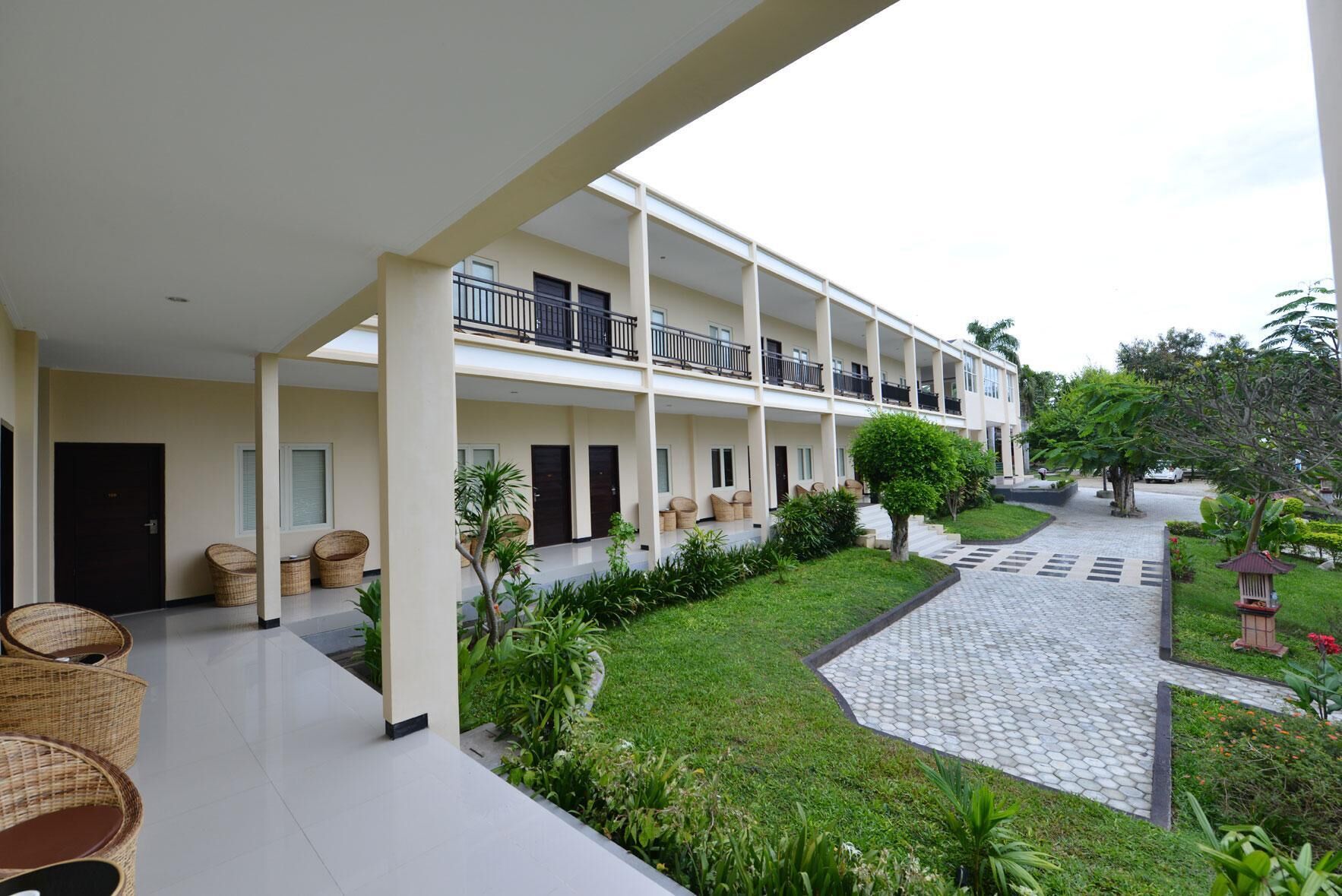 Um hotel com vários andares, com área externa coberta, incluindo uma varanda com móveis de vime e um caminho de jardim.