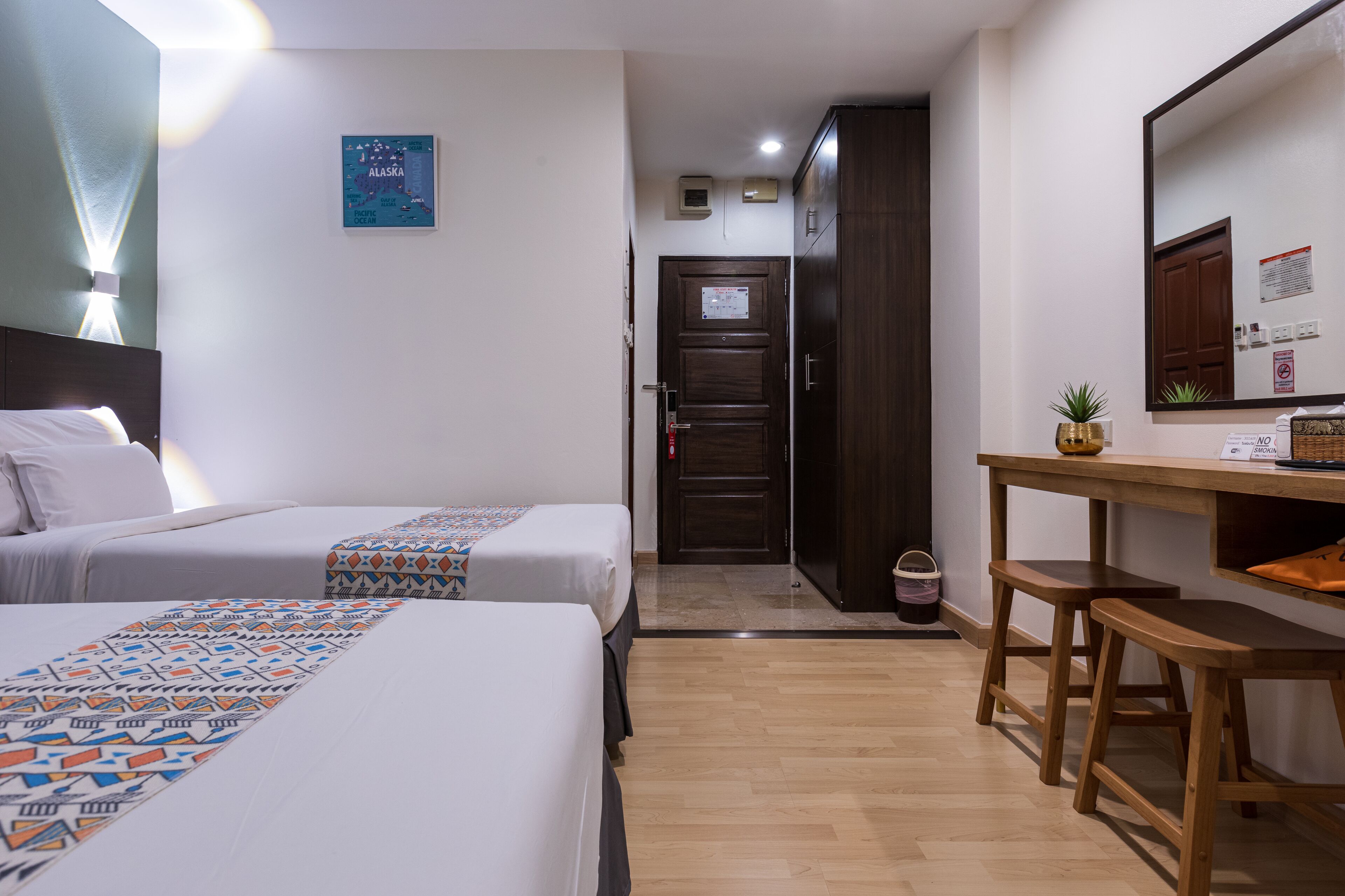 Quarto de hotel com duas camas, uma escrivaninha de madeira, um espelho e um mapa na parede.