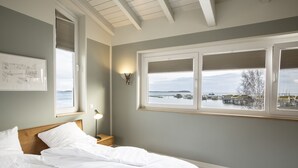 Quarto com uma cama grande, mesa de cabeceira, luminária na parede e janela com vista para a água e os cais.