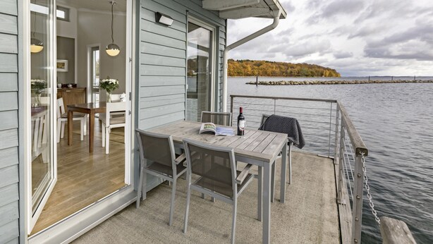 Um deck de madeira com mesa e cadeiras, uma área de refeições com mesa e cadeiras, e vista para um lago com um píer.