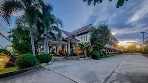 Um hotel com área externa coberta, palmeiras e um pôr do sol ao fundo.