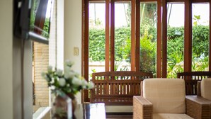 Quarto com um banco de madeira, uma cadeira de vime e vista para o verde lá fora.