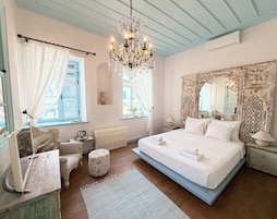Quarto com cama grande, lustre, espelho decorativo e janela com cortinas.
