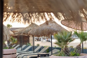 Uma área à beira da piscina com espreguiçadeiras e toldos de palha.