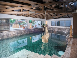 Piscina interna com água cristalina, vigas de madeira e plantas em vasos.