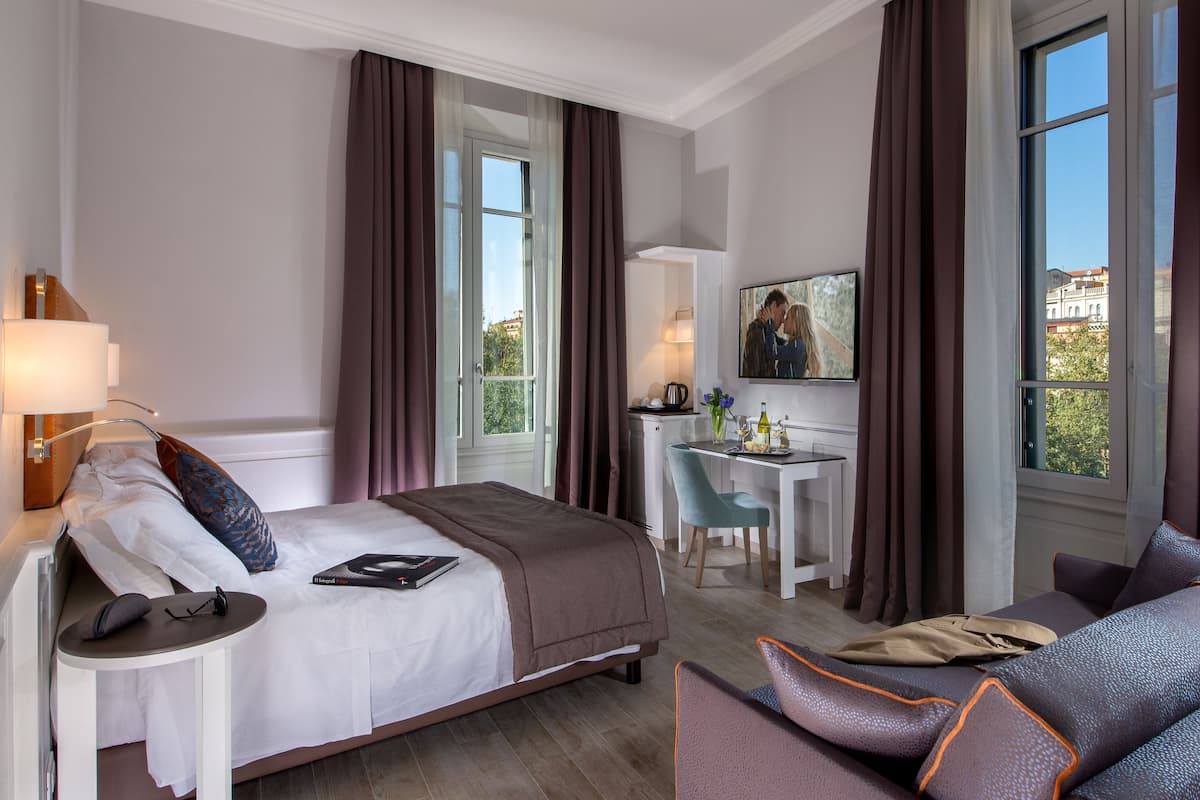 Quarto de hotel com cama, escrivaninha, sofá e vista da cidade.