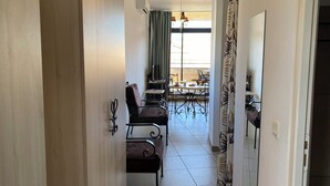 Corredor que leva a uma sala de jantar, com mesa e cadeiras, luminária pendente e vista pela janela.