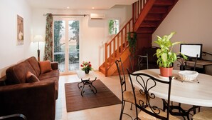 Uma sala de estar com um sofá marrom, uma mesa de jantar com cadeiras, uma escada e um vaso de plantas.
