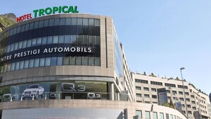 Um hotel chamado "HOTEL TROPICAL" com uma placa para "CENTRE PRESTIGI AUTOMOBILS" abaixo.