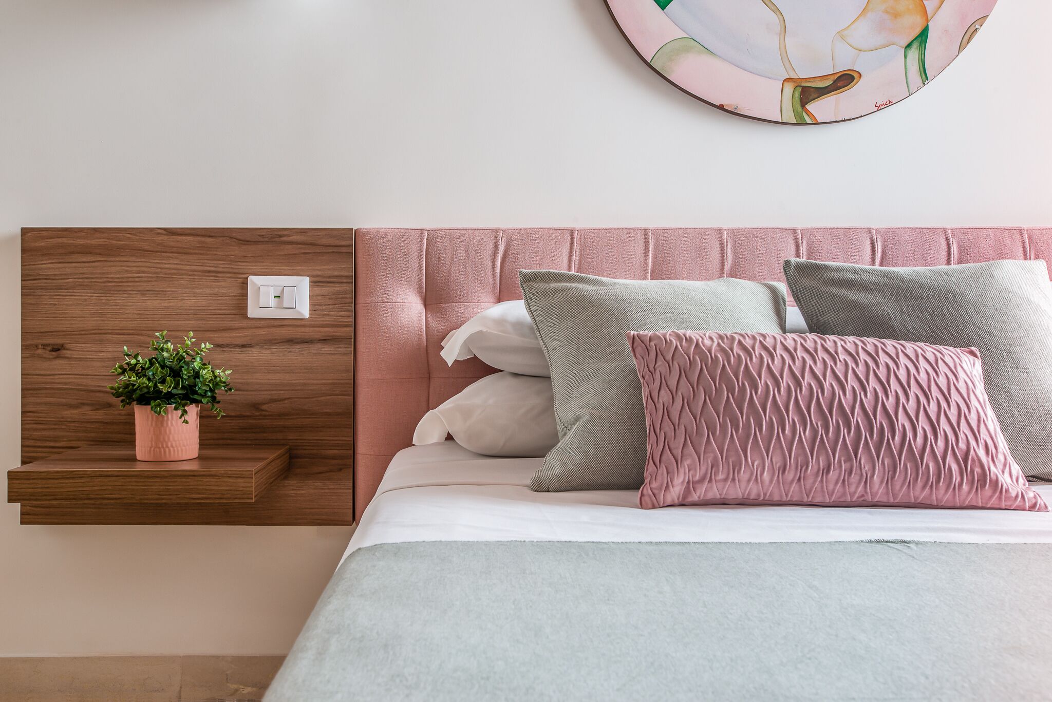 Quarto com cabeceira de madeira, mesa de cabeceira com uma planta e cama com travesseiros e cobertor.
