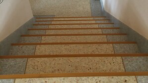 Escada com corrimão, degraus revestidos de carpete e piso cerâmico.