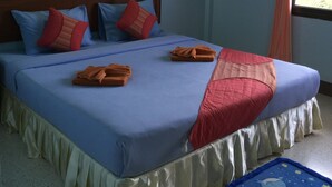 Cama bem arrumada com roupa de cama azul e vermelha, cabeceira de madeira e uma janela com cortinas.