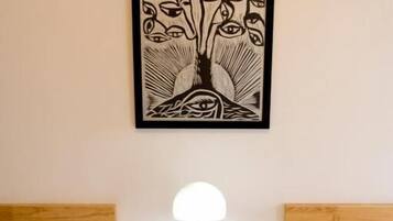 Quarto com duas camas, uma mesa de cabeceira com abajur e uma obra de arte emoldurada na parede.