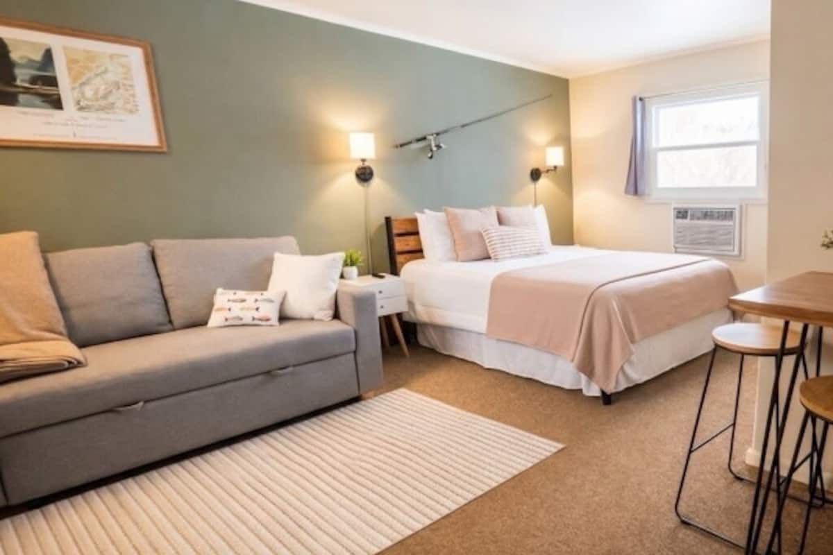 Quarto com cama, sofá, uma mesinha e janela.