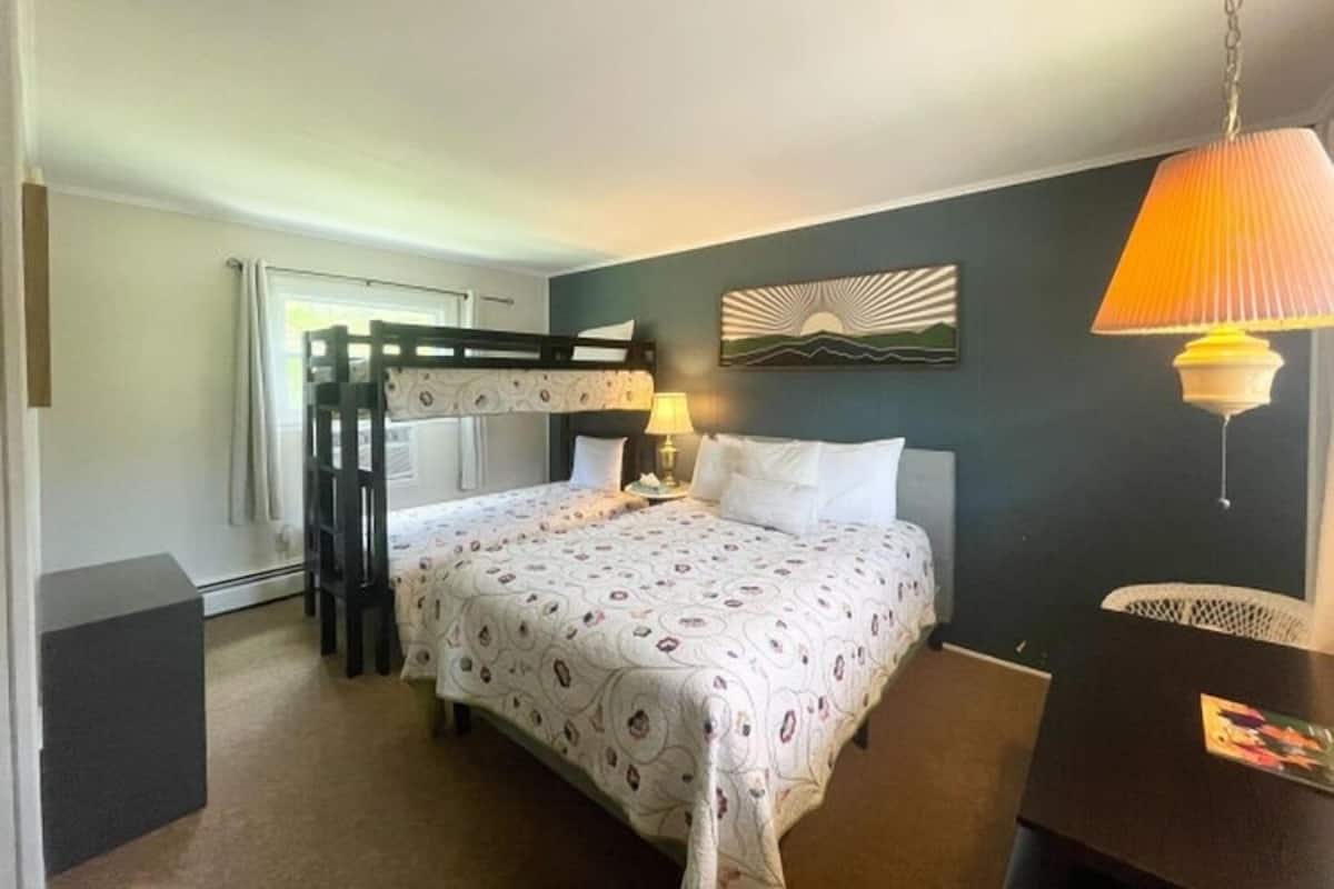 Quarto com uma cama beliche, uma mesa de cabeceira com abajur e uma obra de arte pendurada na parede.