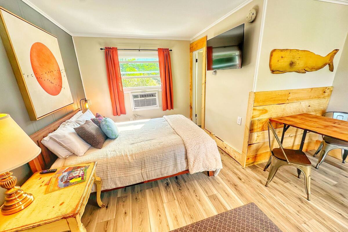 Quarto com cama, mesa de cabeceira, luminária e um banco de madeira.