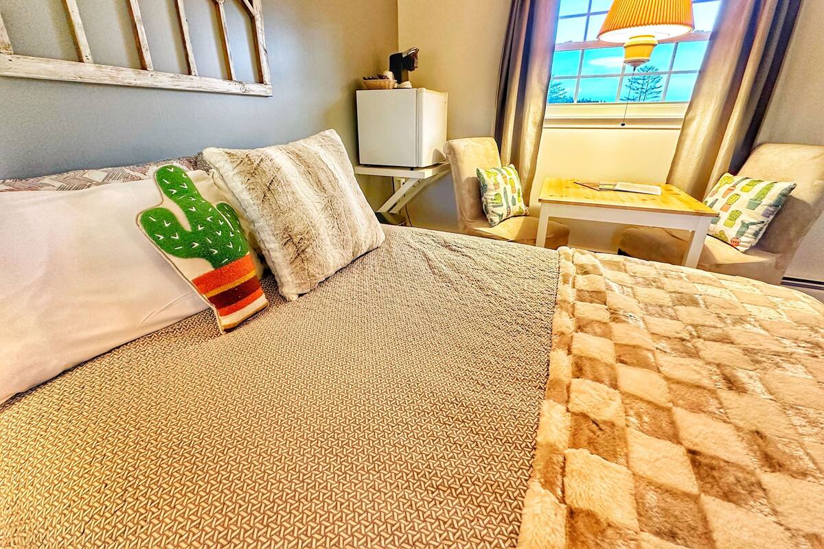 Quarto de hotel com cama, escrivaninha, cadeira e janela com cortinas.