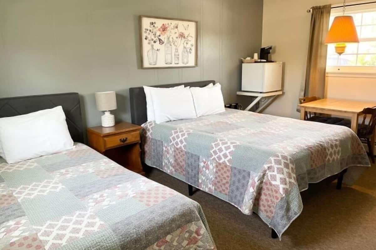 Quarto de hotel com duas camas, uma escrivaninha, uma cadeira, uma televisão e um quadro na parede.