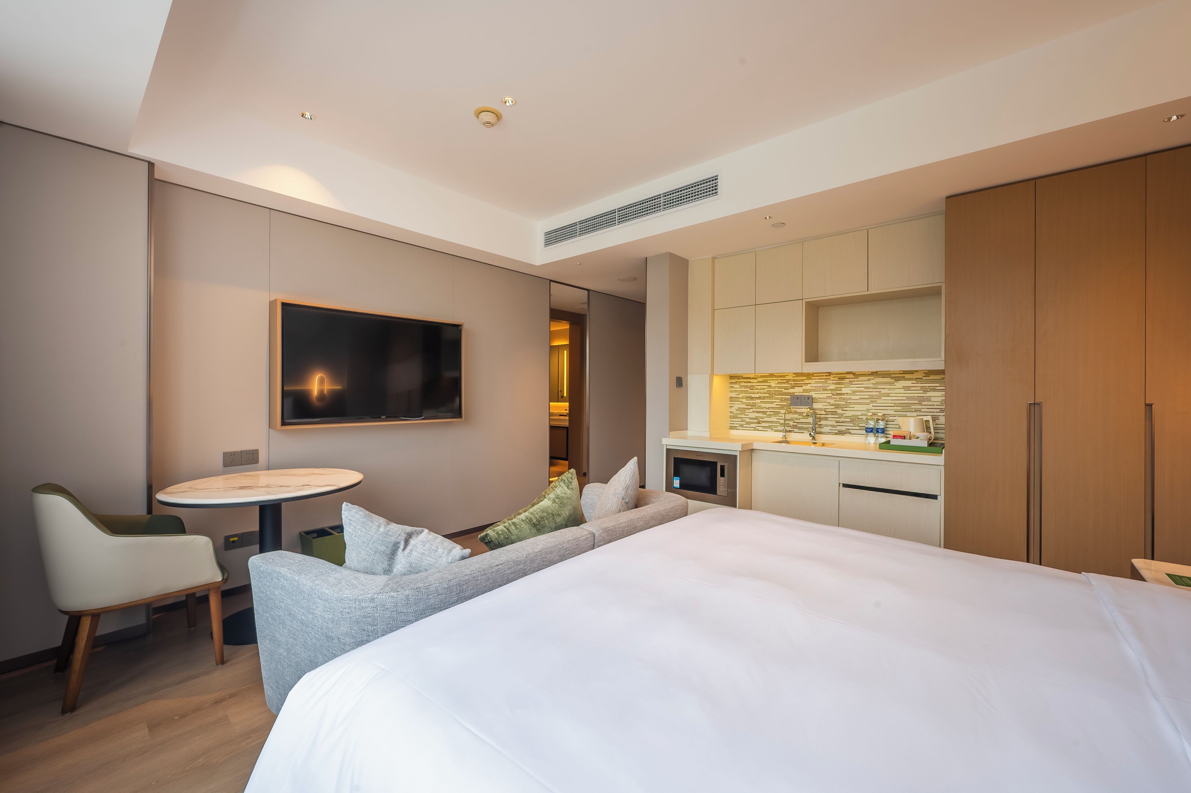 Quarto de hotel moderno com uma cama grande, uma escrivaninha, uma cadeira, uma televisão, uma cozinha compacta e um banheiro.