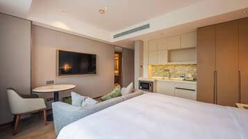 Quarto de hotel moderno com uma cama grande, uma escrivaninha, uma cadeira, uma televisão, uma cozinha compacta e um banheiro.