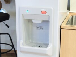 Dispensador de água com botão de energia e botão de pressão, localizado ao lado de uma pia em uma cozinha.