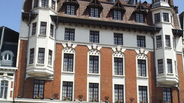 Um edifício histórico com uma torre de esquina, janelas amplas e uma placa com o nome Hotel Le Vieux Beffroi.
