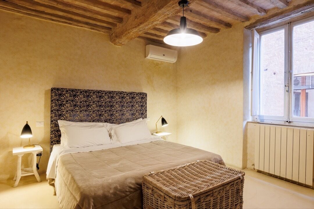 Quarto com cama, luminárias de cabeceira, cesto de vime, janela e ventilador de teto.