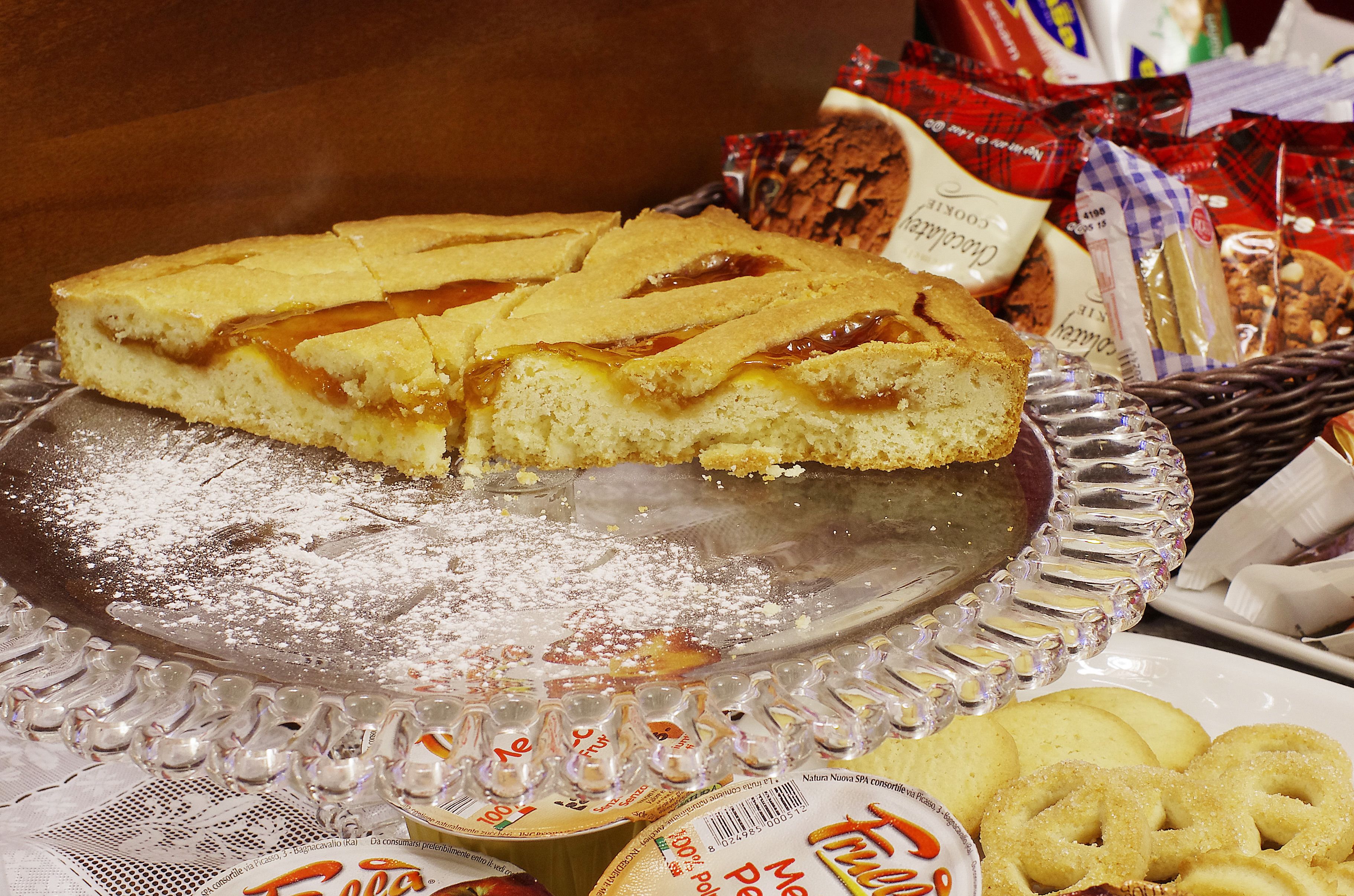 Um prato de sobremesa com uma fatia de bolo, açúcar em pó e um pequeno recipiente de creme.
