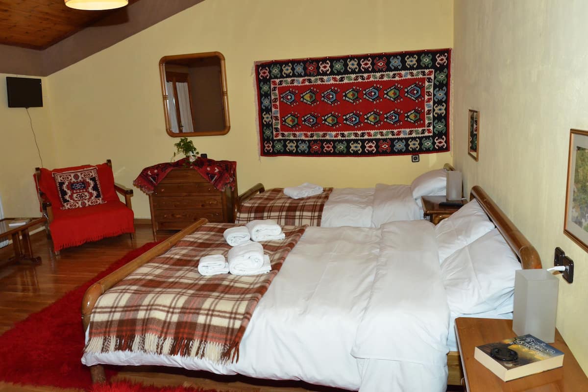 Quarto de hotel com duas camas, uma poltrona vermelha, cómoda de madeira e um tapete decorativo grande.