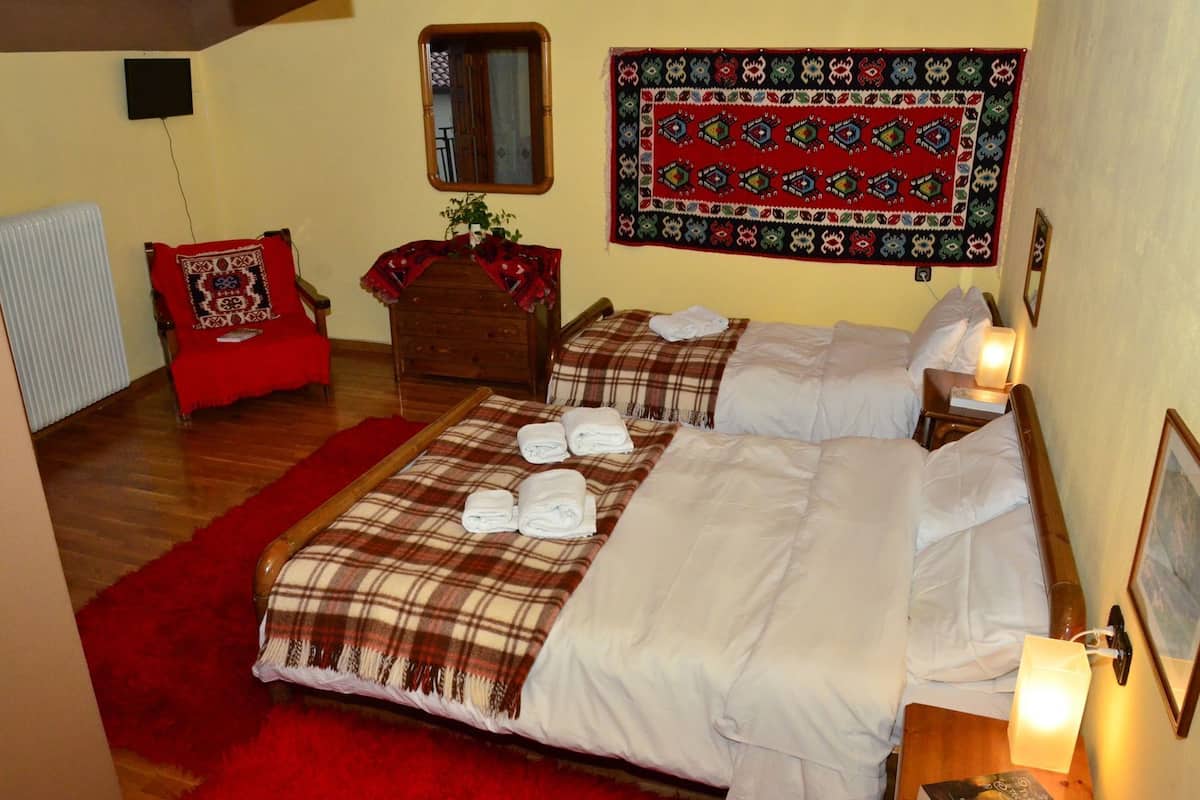 Quarto de hotel com duas camas, um tapete vermelho, uma cômoda de madeira, um espelho e uma tapeçaria na parede.