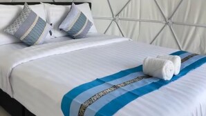 Cama bem arrumada com lençóis brancos, manta azul e branca listrada e dois travesseiros.