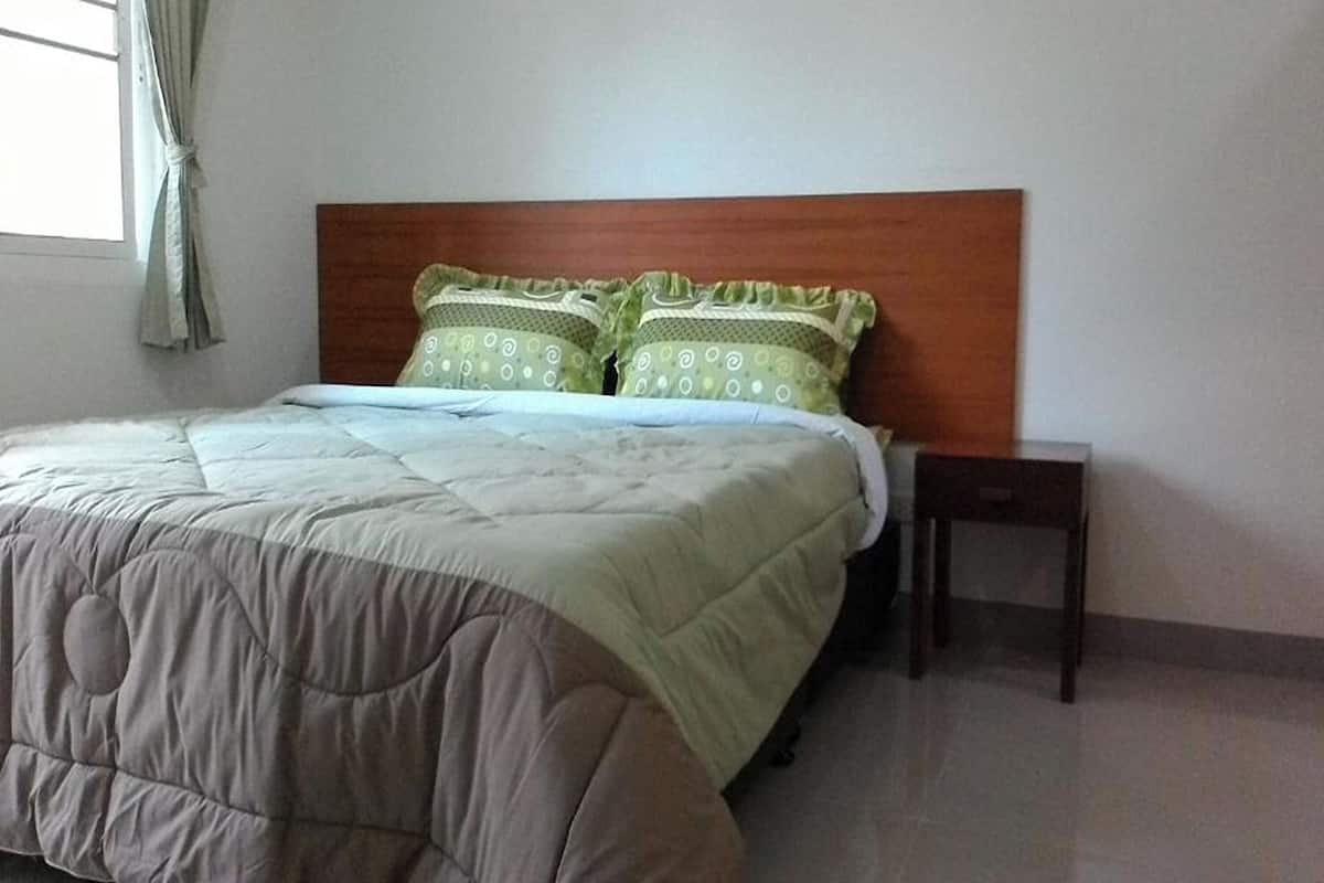 Uma cama bem arrumada com edredom bege e branco, duas almofadas estampadas e uma cabeceira de madeira.