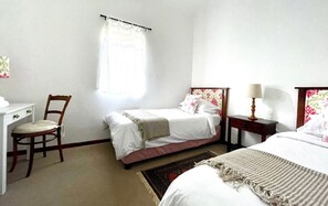 Quarto com uma cama de solteiro, uma cadeira, uma escrivaninha e uma mesa de cabeceira.