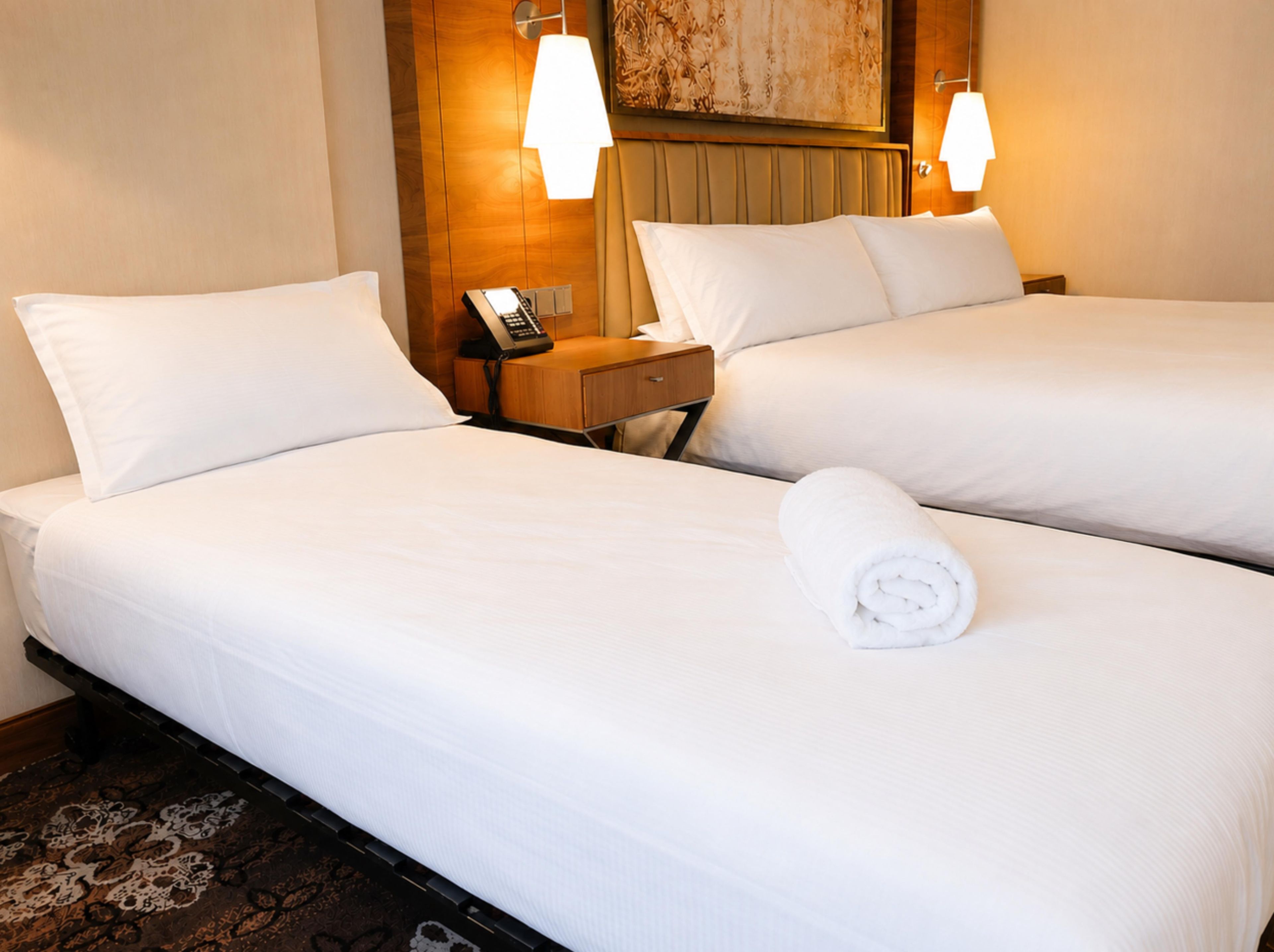 Quarto de hotel com duas camas, um telefone ao lado da cama e uma toalha enrolada em uma das camas.