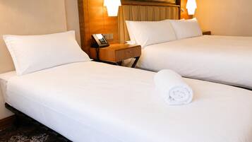 Quarto de hotel com duas camas, um telefone ao lado da cama e uma toalha enrolada em uma das camas.