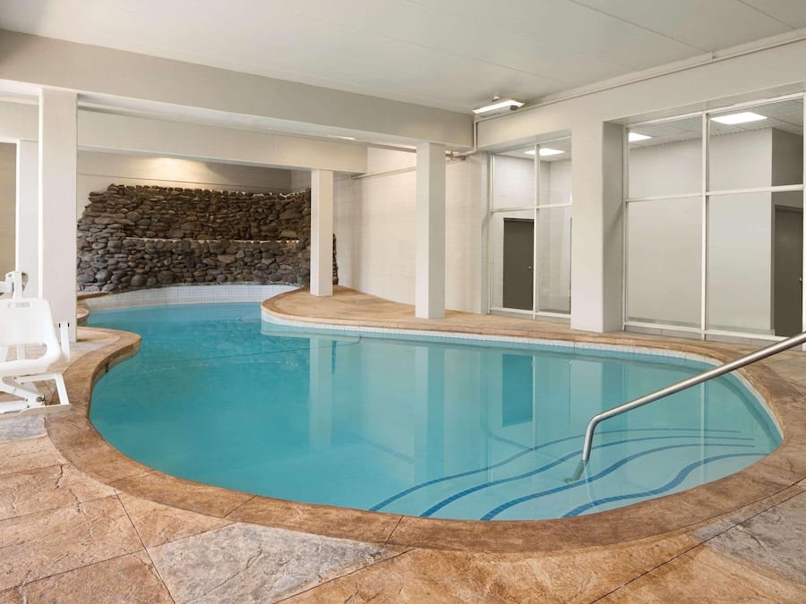 Piscina interior com parede de pedra ao fundo, uma cadeira à beira da piscina e água azul cristalina.