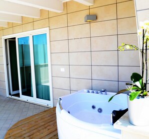 Uma área de spa com hidromassagem, uma planta em vaso e uma porta de vidro deslizante que dá para uma varanda.